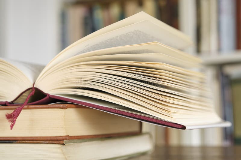 Open Book or Textbook on a Pile of Closed Books in Front of a Bookcase ...