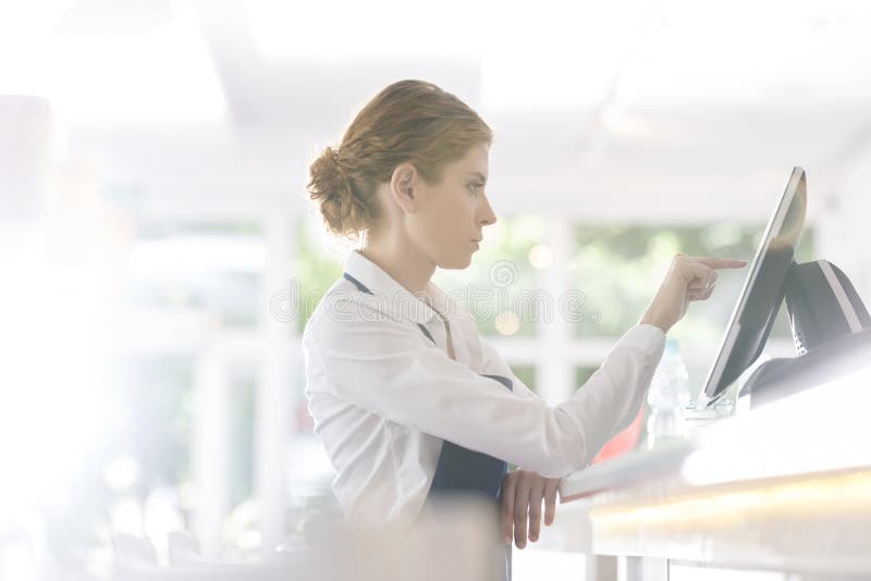 Side View of Confident Young Waitress Using Computer while Standing at ...