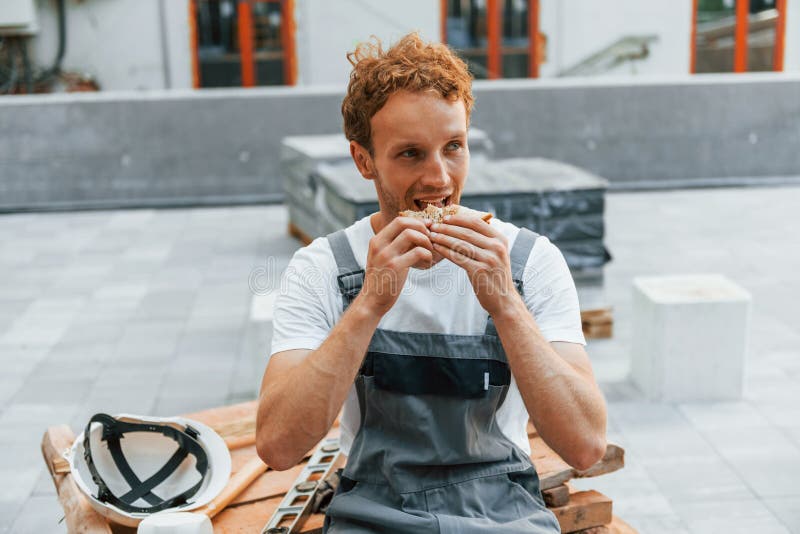 Eating Food. Young Man Working in Uniform at Construction at Daytime ...
