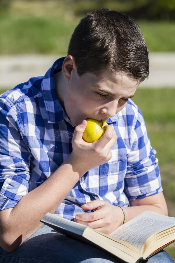 Eating.Young Man Reading a Book in Outdoor with Yellow Apple. Stock ...