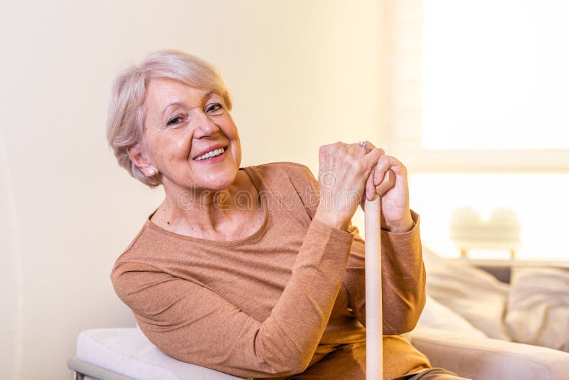 Elder Lady Sitting On The Couch With Wooden Walking Stick And Smiling