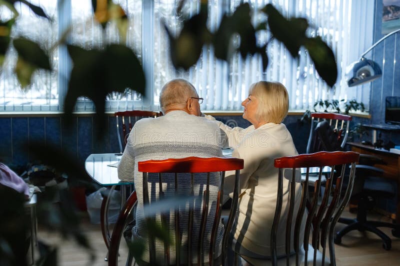 An Elderly Couple is Sitting at a Table, the Woman is Caring for the ...