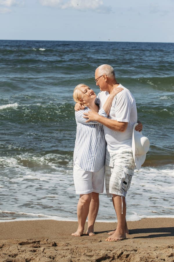 An Elderly Couple Stand Hugging on the Beach by the Sea, Look at Each ...