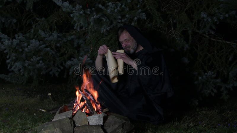 An Elderly Hooded Monk Reads an Ancient Scroll by the Fire at Night ...