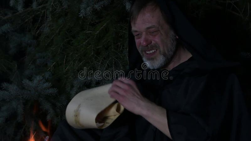 An Elderly Hooded Monk Reads an Ancient Scroll by the Fire at Night ...