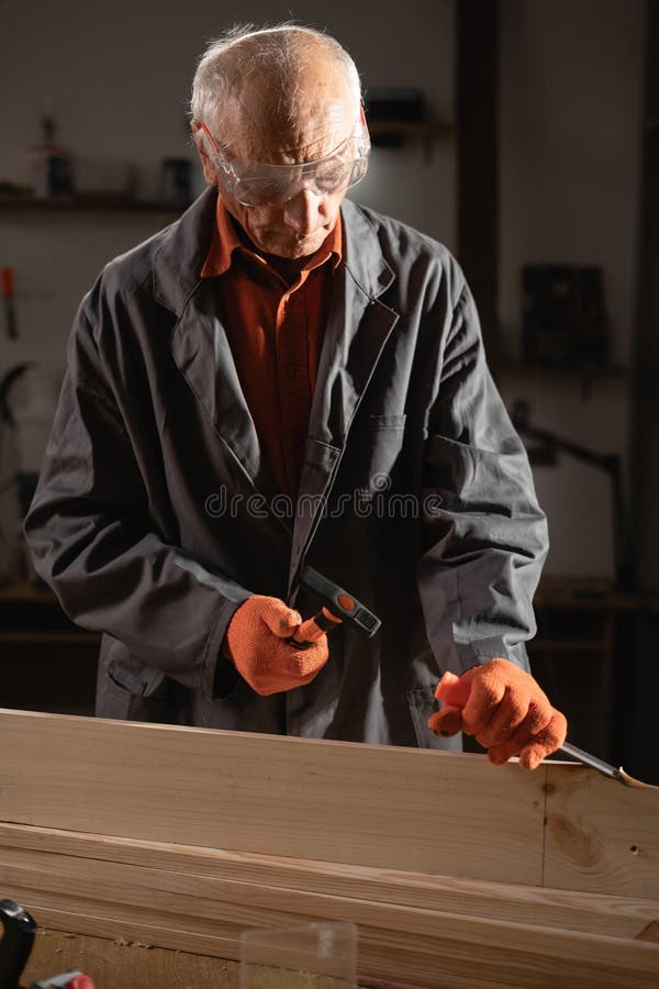 Elderly Male Carpenter Working with Wood Using a Chisel and Hammer in ...