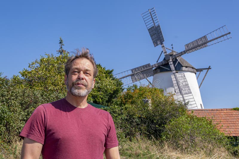An Elderly Man with a Beard Against a Background of a Windmill and a ...