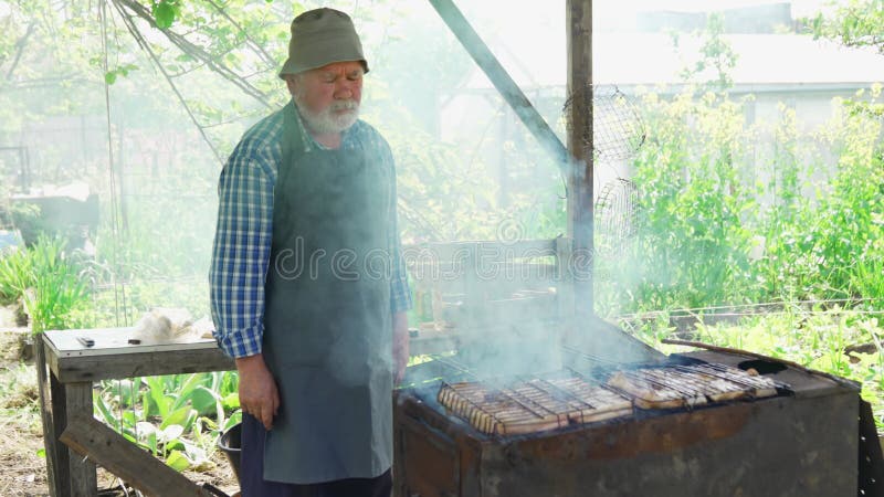 An Elderly Man Frys Meat in a Grill on a Fire on the Grill Stock ...