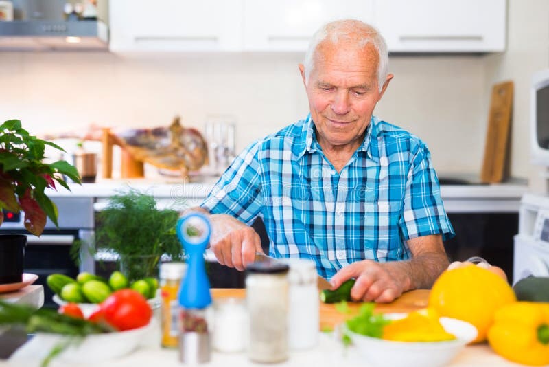 Elderly Man Cuts Vegetables for Salad at the Table in the Kitchen Stock ...