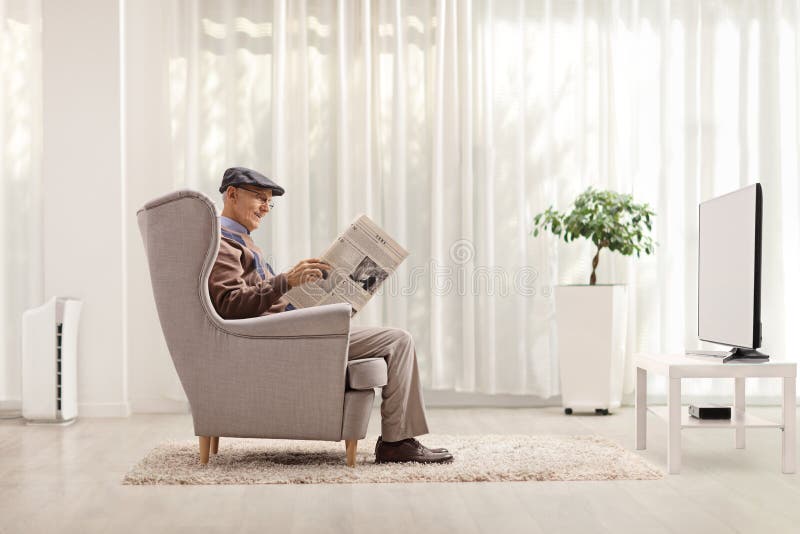 Elderly Man Sitting In An Armchair And Reading A Newspaper In A Living