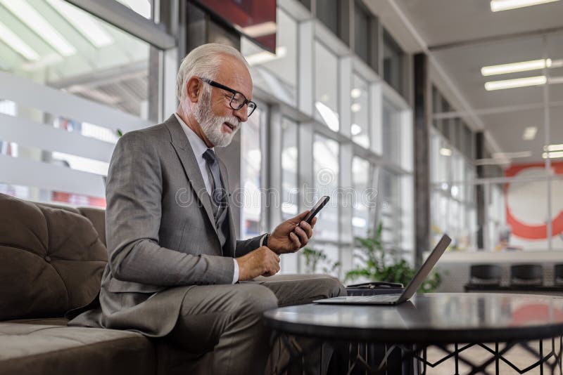 Elderly Professional Networking on Mobile Phone while Using Laptop at ...