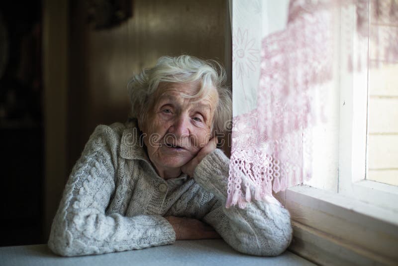 An Elderly Sad Woman Sitting at a Table in the House. Stock Image ...