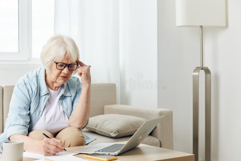 An Elderly Woman is Sitting at Home on a Cozy Sofa, Working Intently in ...