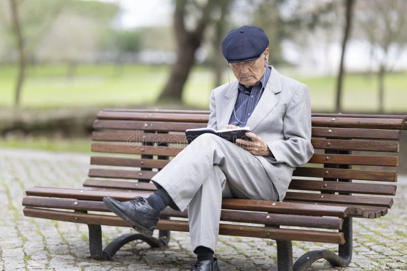 Elderly Writer Taking Notes in a Notebook while Sitting on a Bench in ...