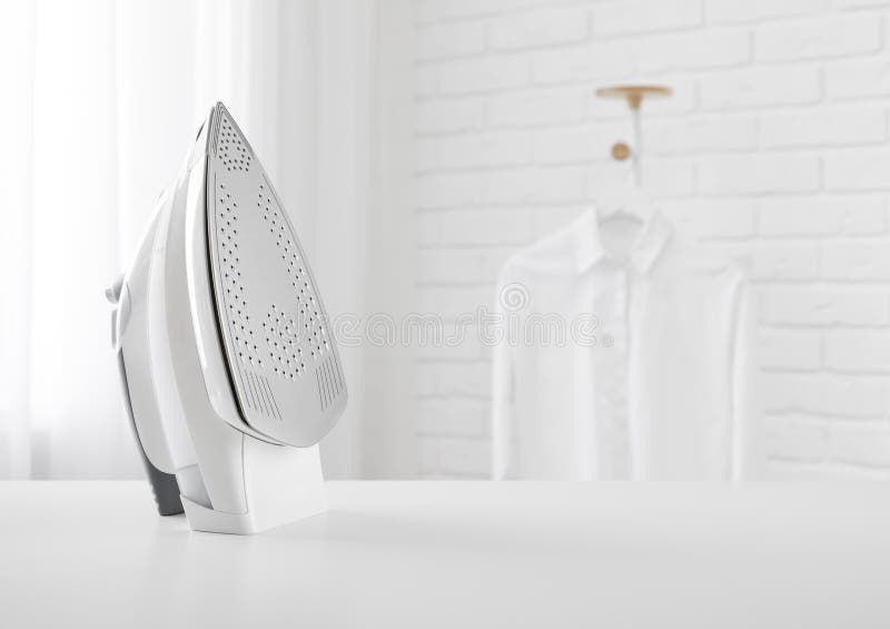 Electric Iron on Table in Blurred Room with Clothes Rack Stock Image ...