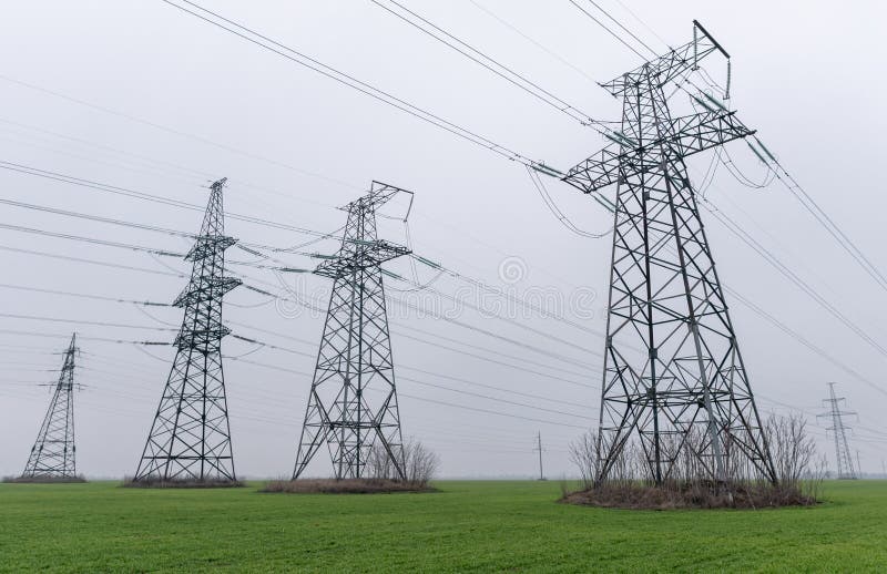 Electric Network of Pylons Against a Cloudy Sky and a Green Meadow ...