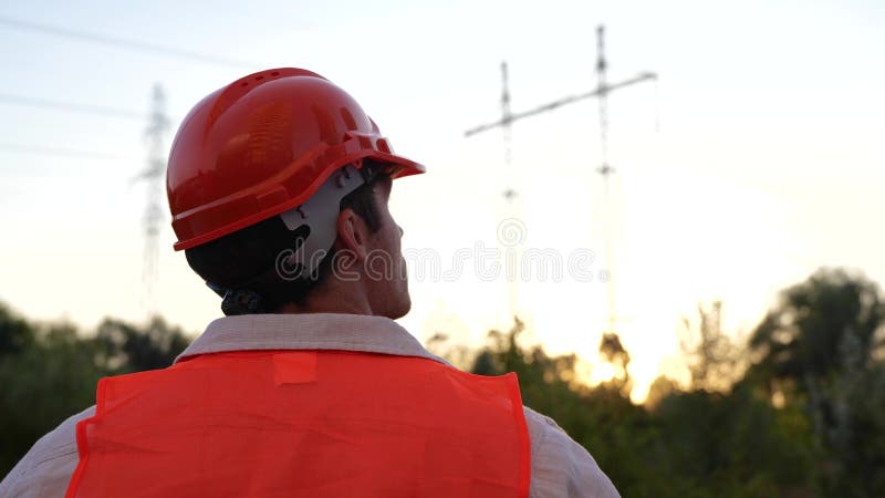 Young Engineer Standing Outdoors while Looking at the High Voltage ...