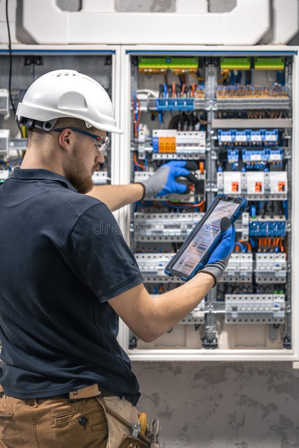 Electrical Technician Working in a Switchboard with Fuses, Uses a Tablet. Stock Image - Image of ...