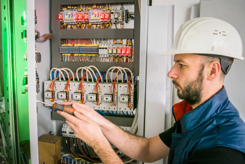 An Electrician in a Helmet Connects the Wires of the Circuit Breakers ...
