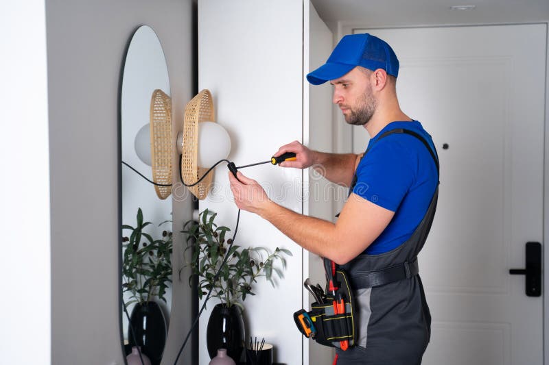 An Electrician Man in a Work Uniform Repairs a Lamp in the Corridor ...