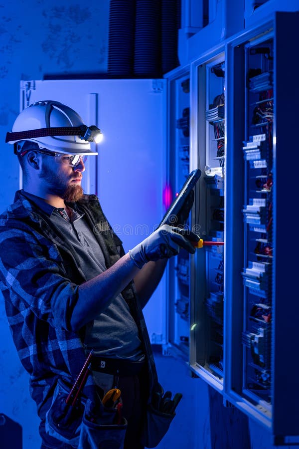 Electrician in Overalls, Focused on Work in Switchboard with Fuses ...