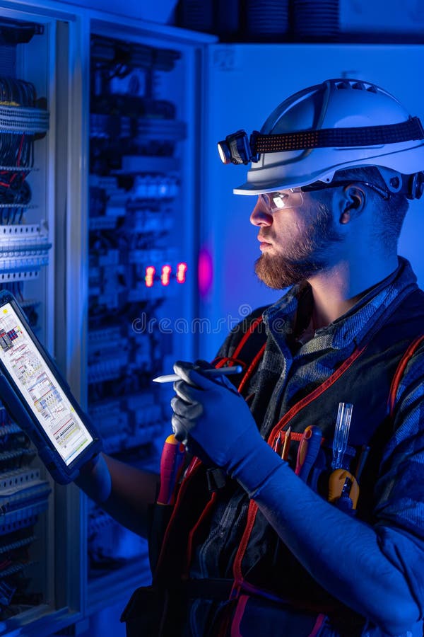 Electrician in Overalls, Focused on Work in Switchboard with Fuses ...