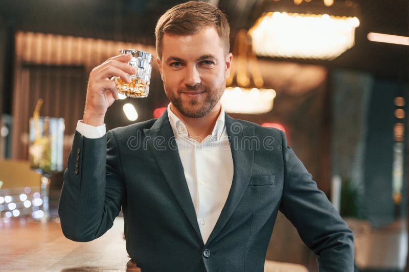 An Elegant Man in Black Suit is in the Bar, Tasting the Alcohol Drink ...