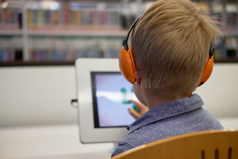 Elementary School Boy Sitting in Library, Using Touchscreen Computer ...
