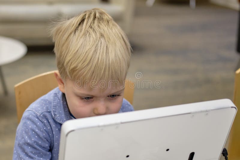 Elementary School Boy Sitting in Library, Using Touchscreen Computer ...