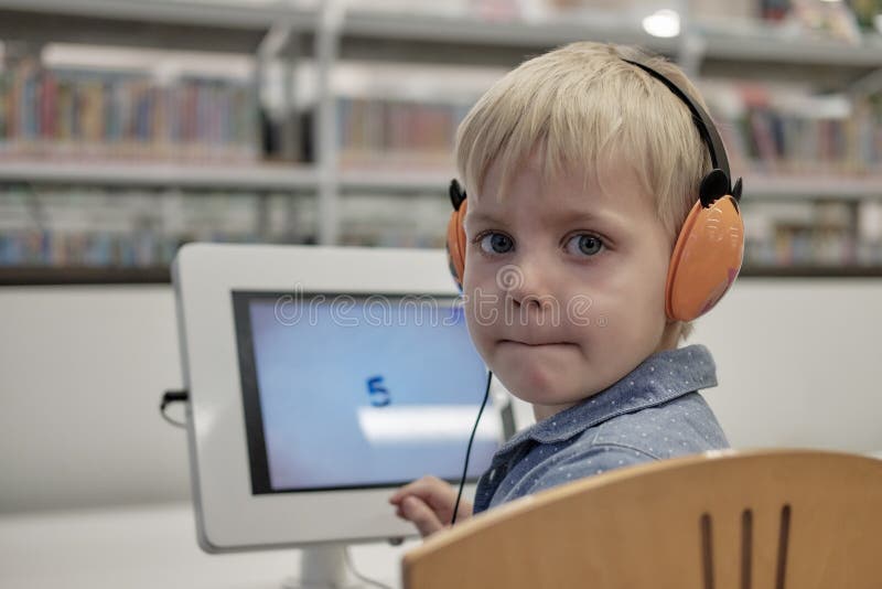 Elementary School Boy Sitting in Library, Using Touchscreen Computer ...