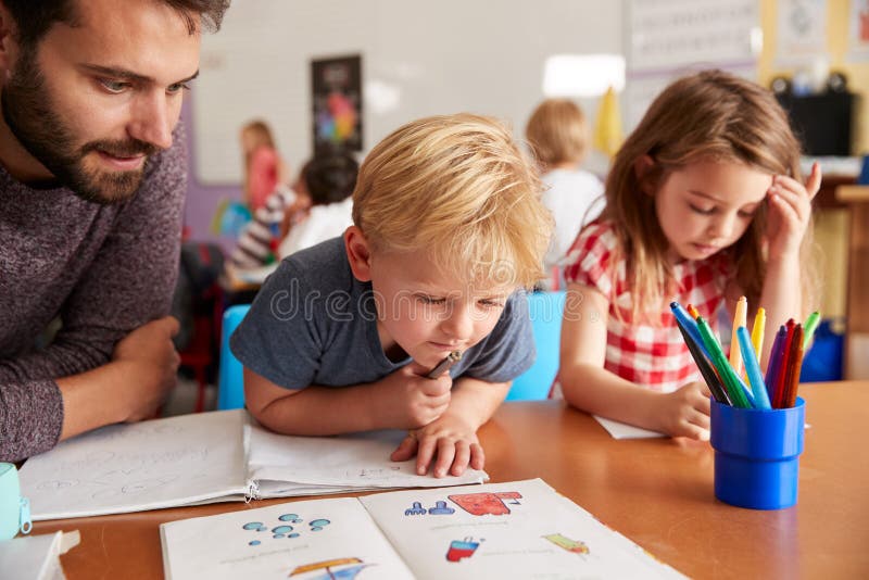 Elementary School Teacher Helping Pupils As they Work at Desk in ...