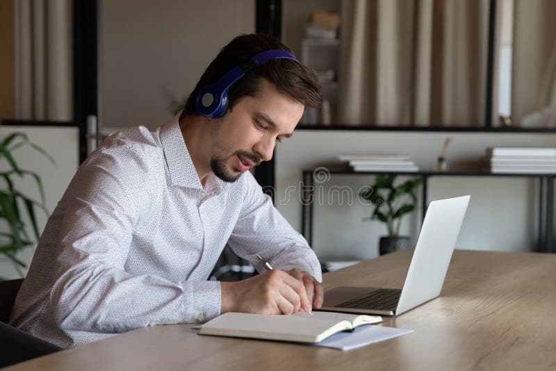Employee In Headphones Taking Notes Watching Webinar In Office Stock