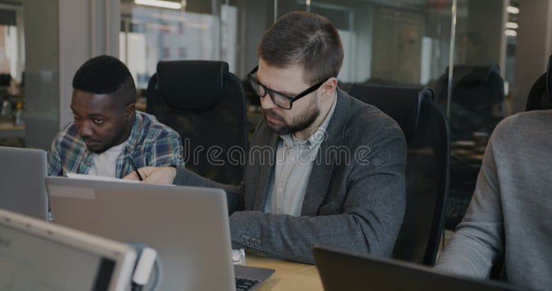 Employees Working with Laptops Typing and Talking To Colleagues Reading ...
