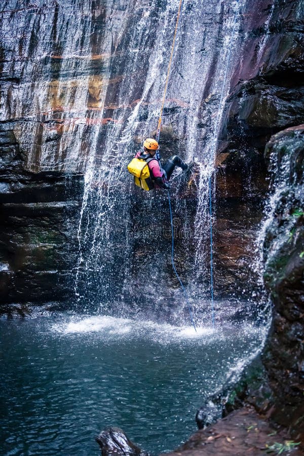 Man Abseiling Down Cascading Waterfall into Deep Pool, Wearing Backpack ...