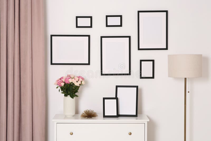 Empty Frames Hanging on White Wall and Chest of Drawers with Flowers ...
