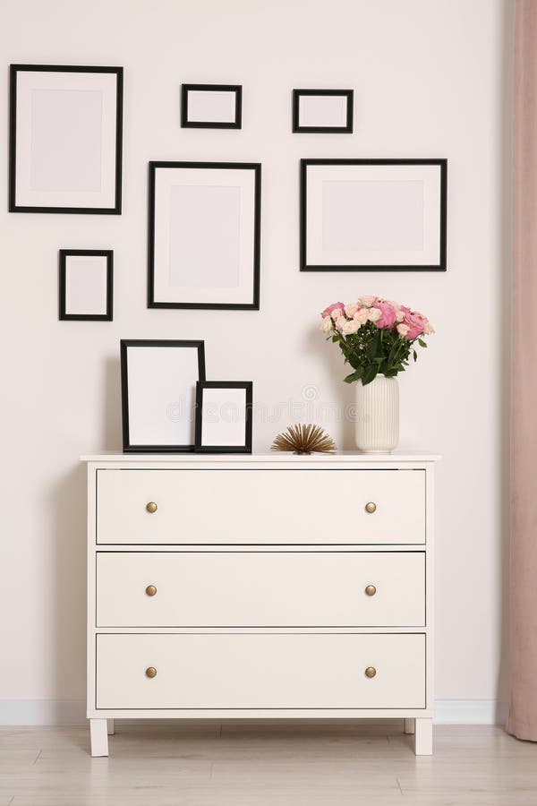 Empty Frames Hanging on White Wall and Chest of Drawers with Flowers in ...