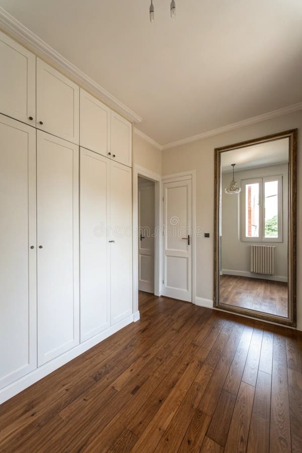 An Empty Room with Wood Floors and White Cupboards on the Left Side of ...