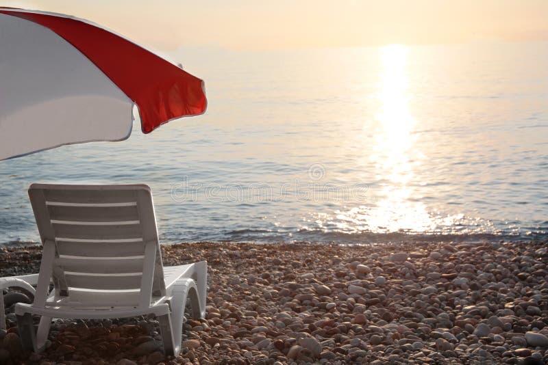 Empty Sunbed and Umbrella on Stone Beach Near Sea at Sunset Stock Photo ...