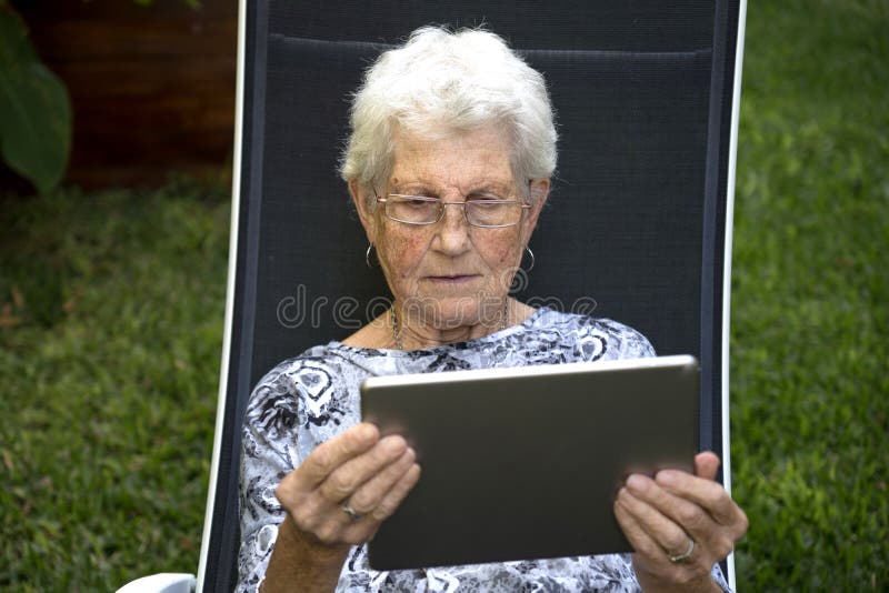 En Gammal Dam Som Sitter På En Barnstol Och Läser Från En Tablett I