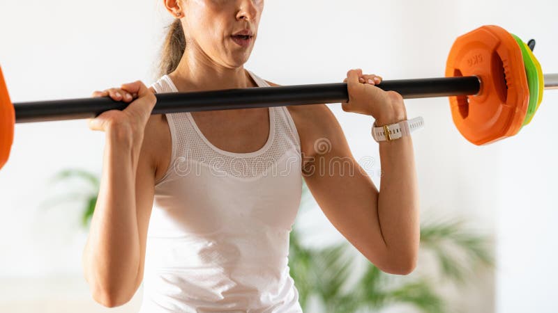 Engaging in a Home Workout, a Woman Utilizes a Barbell Bar with Weights ...