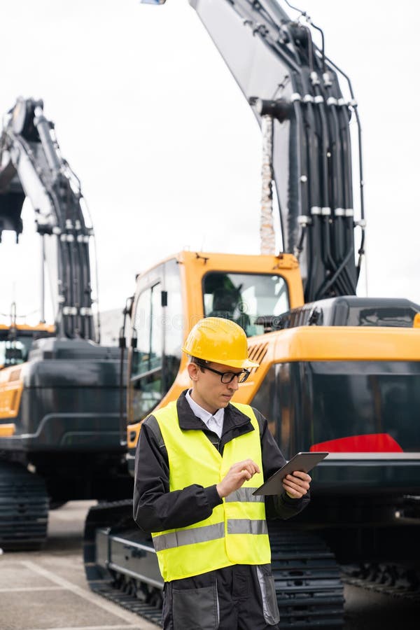 Engineer with a Digital Tablet Stands Next To Construction Excavators ...