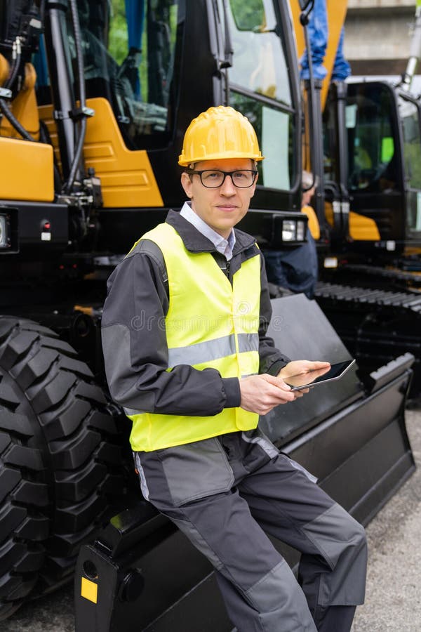 Engineer in a Helmet with a Digital Tablet Stands Next To Construction ...