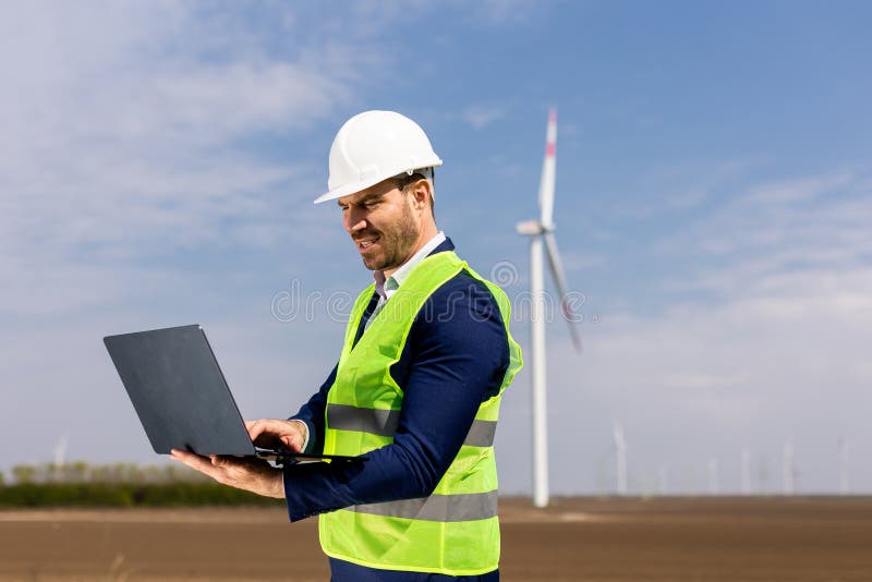 Engineer in High-Visibility Vest Analyzing Data on Laptop at Wind Farm ...
