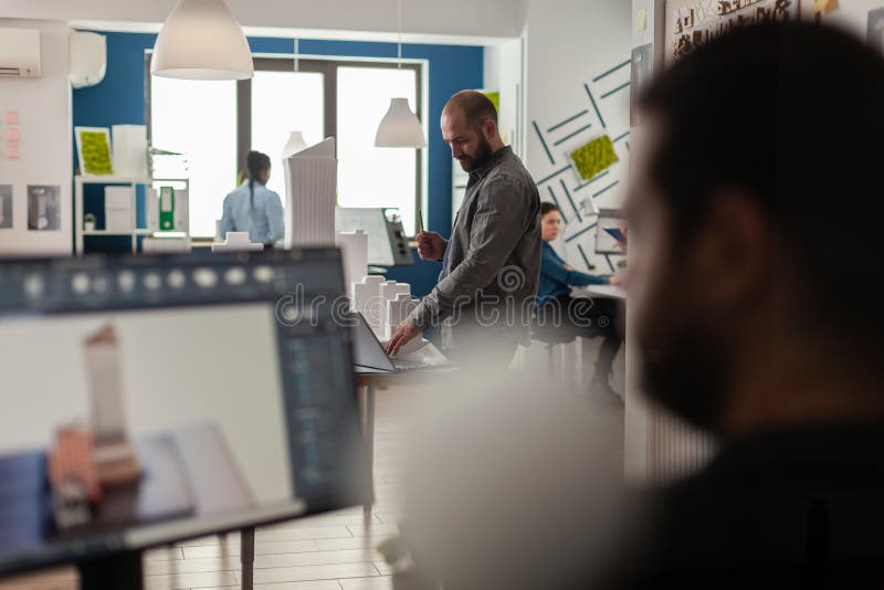 Engineer Looking at Blueprints on Laptop at Desk with Architectural ...