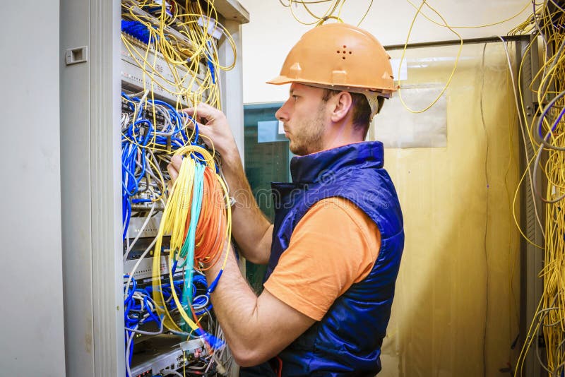 An Engineer in an Orange Helmet Mounts Wires in a Switching Rack. the ...