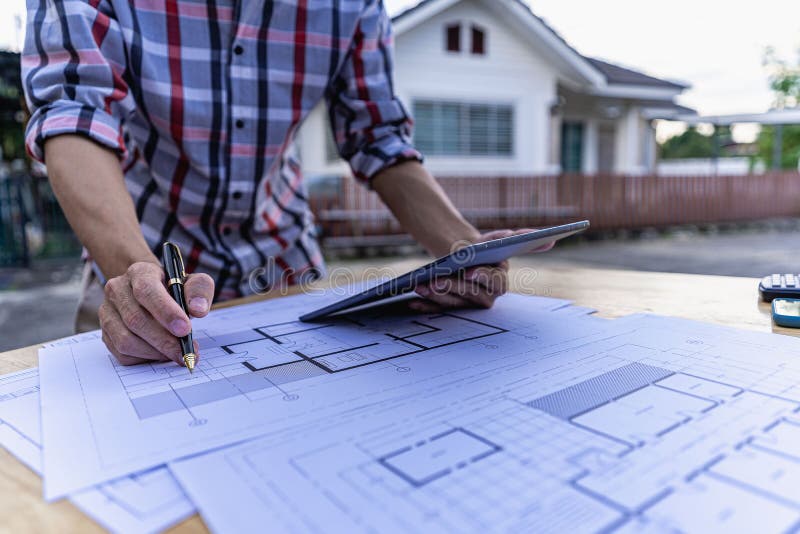 Engineer Pointing at Blueprint and Using Laptop To Draw Building Design ...