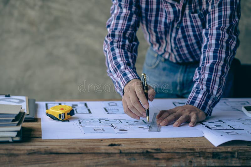 Engineer Pointing at Blueprint and Using Laptop To Draw Building Design ...