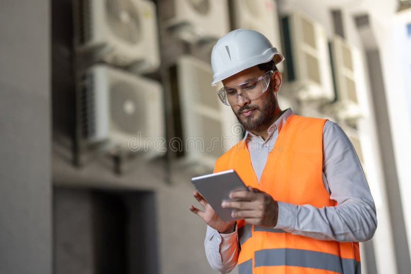 An Engineer in Safety Gear Reviews Data on a Tablet while Working on a ...