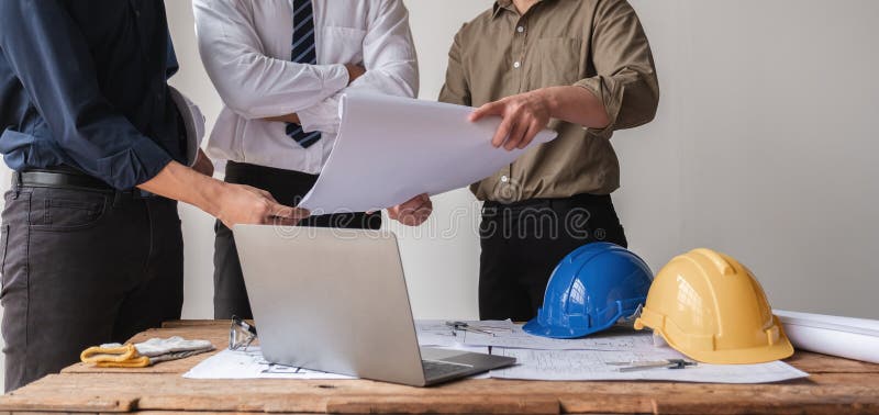 Engineering Team Collaborating on Work Plans at Table with Blueprints ...