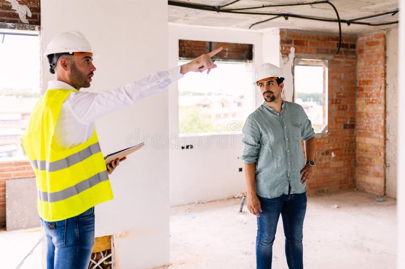 Engineers Discussing Blueprint Wearing Hardhats at Construction Site ...